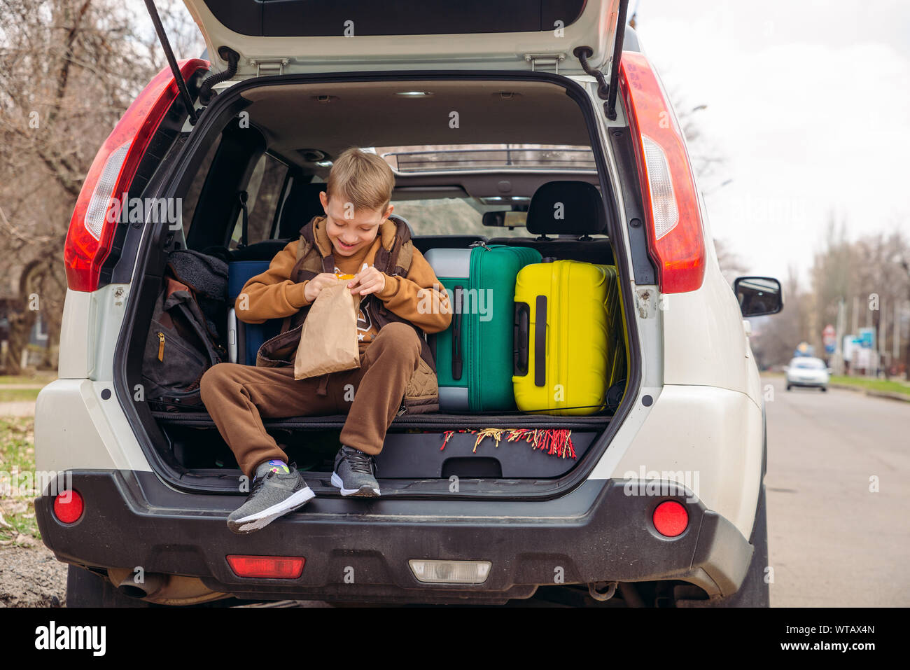 little kid looking into paper bag with candies sitting in car trunk ...