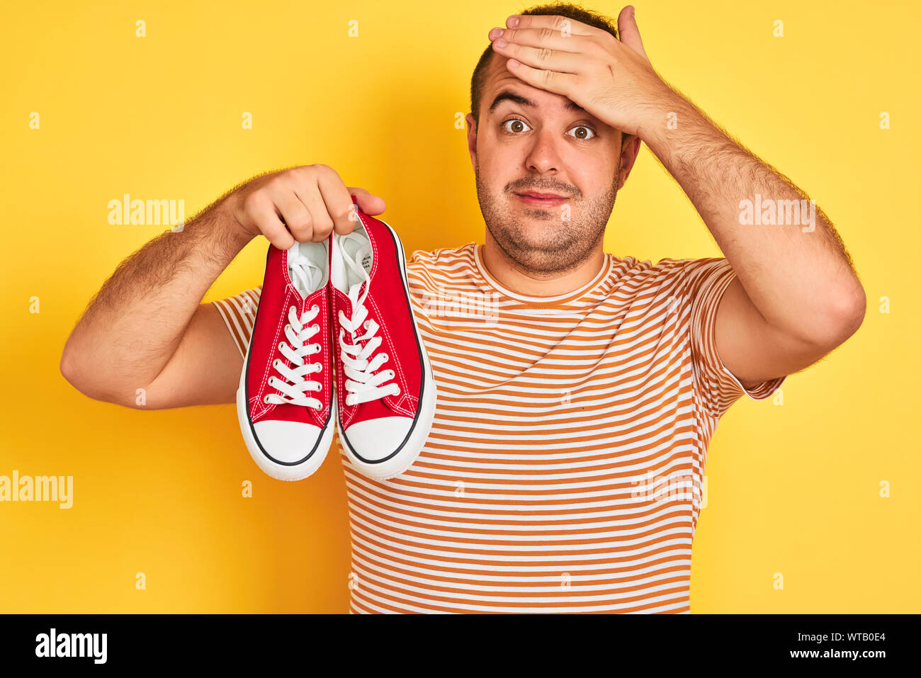 Young man holding red casual sneakers standing over isolated yellow ...
