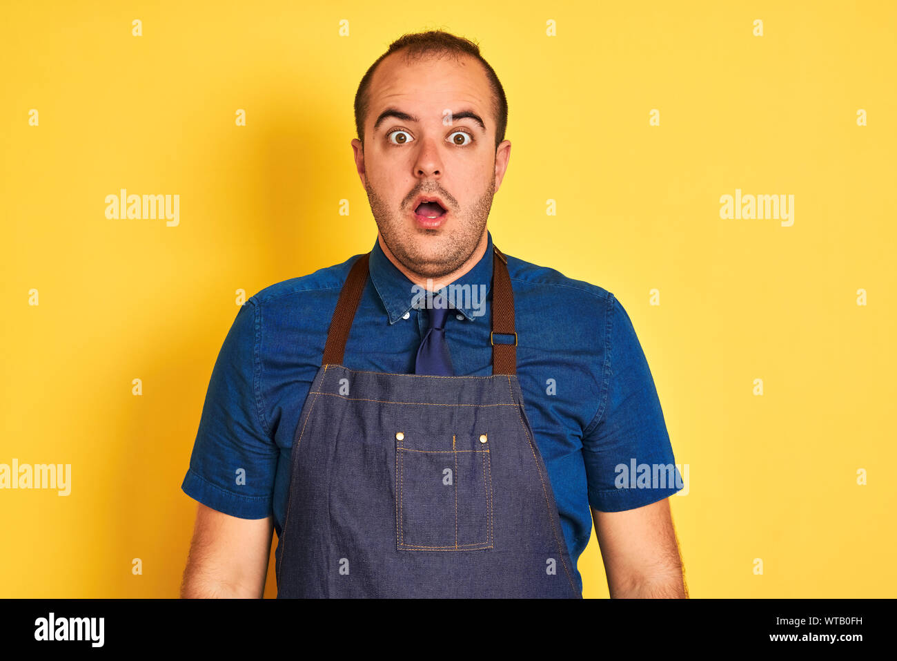 Young shopkeeper man wearing apron standing over isolated yellow ...
