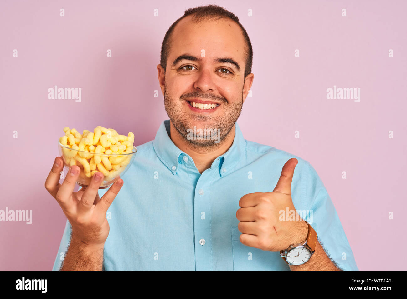 Young man holding bowl with extruded corn standing over isolated pink ...