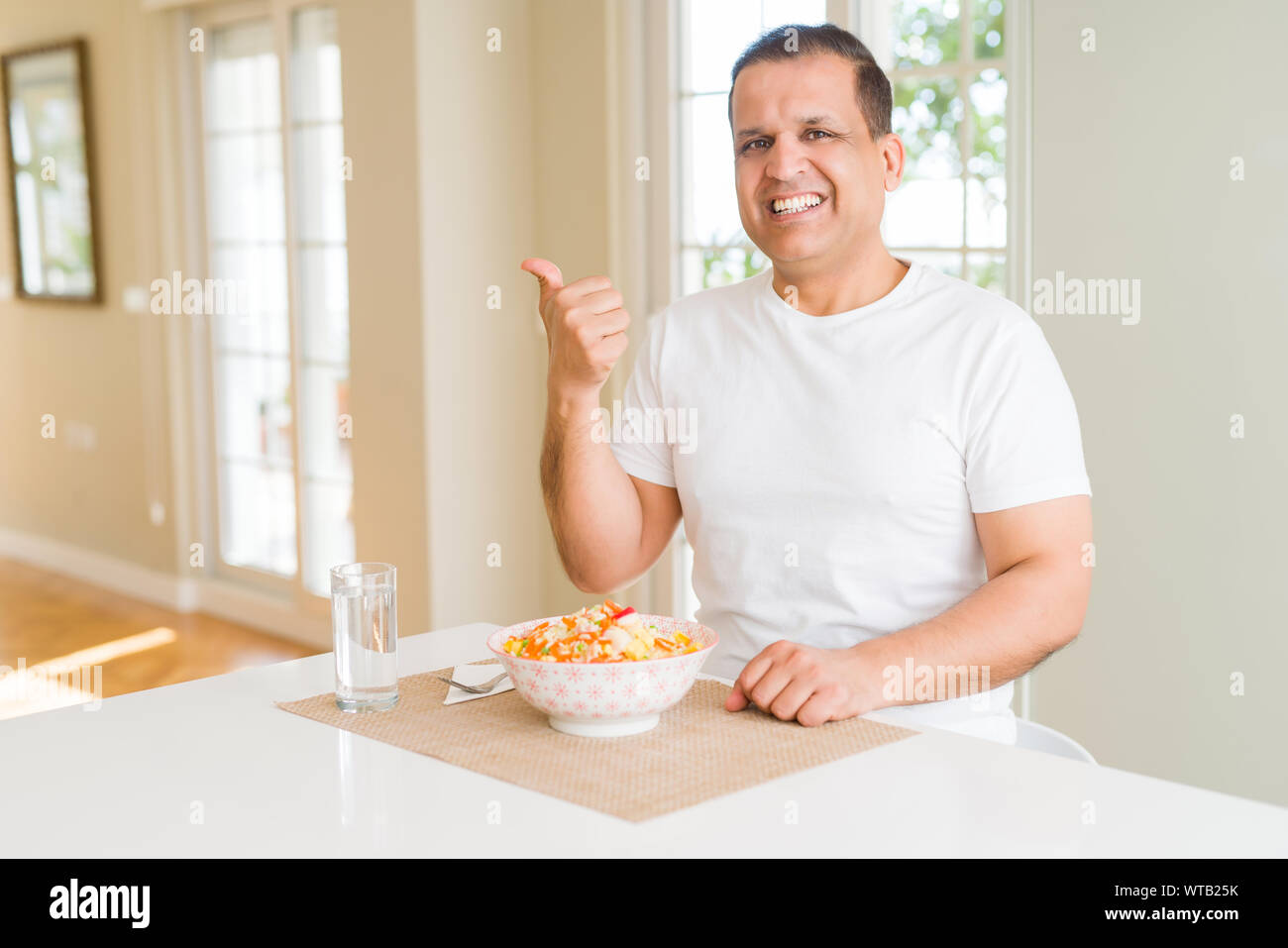 Middle age man eating rice at home smiling with happy face looking and ...