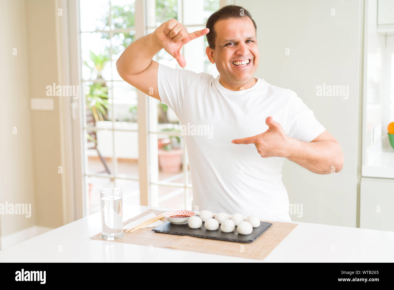 Middle age man eating asian dumplings at home smiling making frame with ...