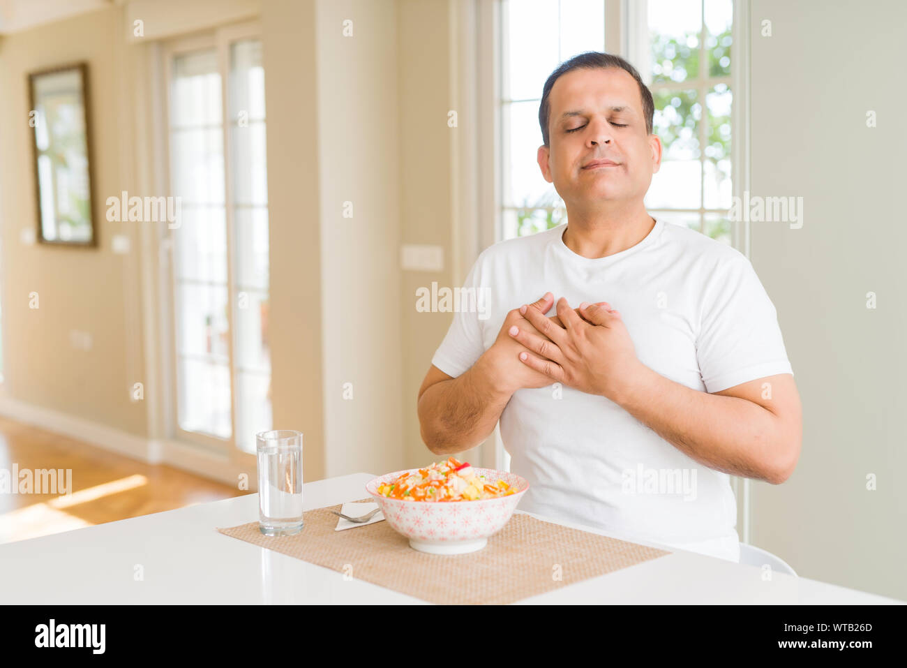 Middle age man eating rice at home smiling with hands on chest with ...