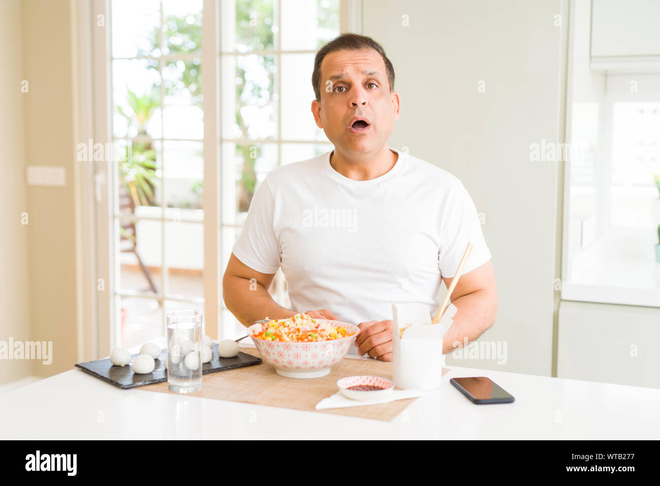Middle age man eating asian food with chopsticks at home afraid and ...