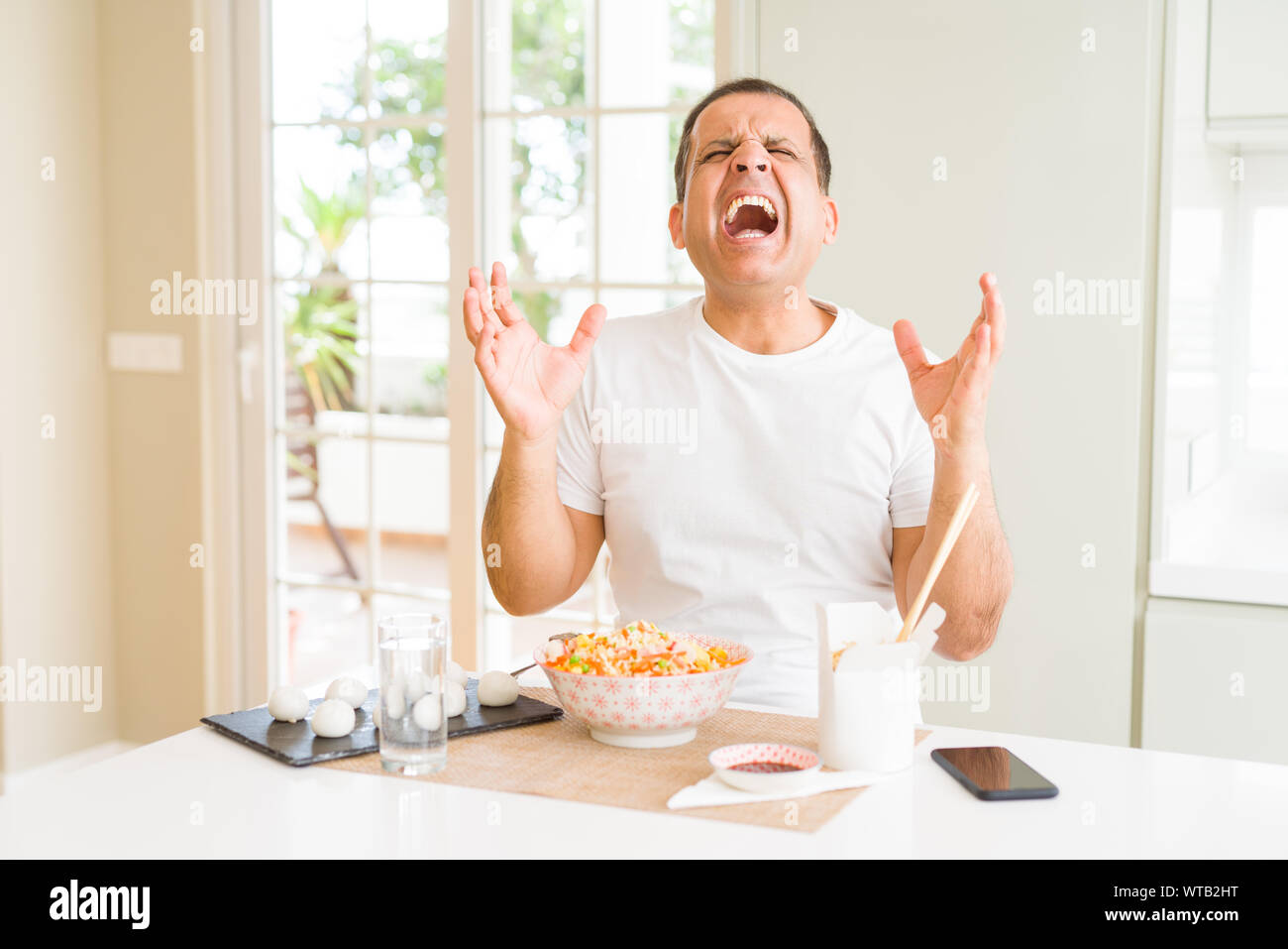 Middle age man eating asian food with chopsticks at home celebrating ...