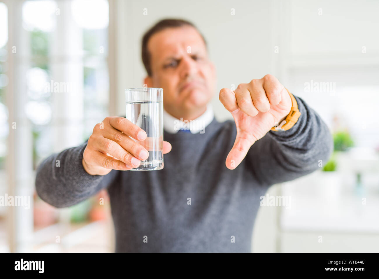 Middle age man drinking glass of water at home with angry face ...