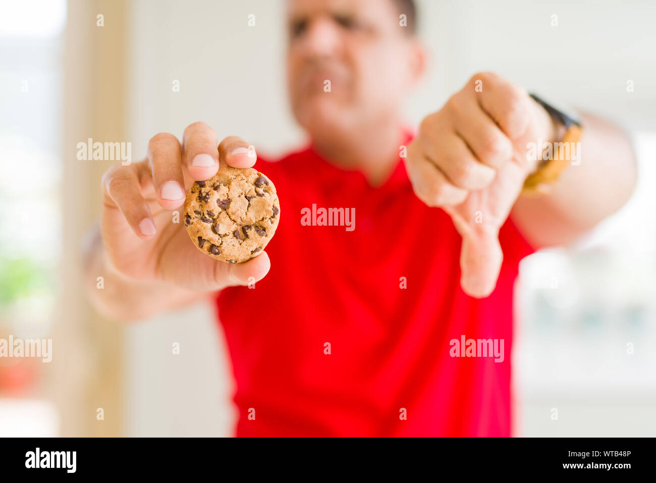 Middle age man eating chocolate chips cookies at home with angry face ...