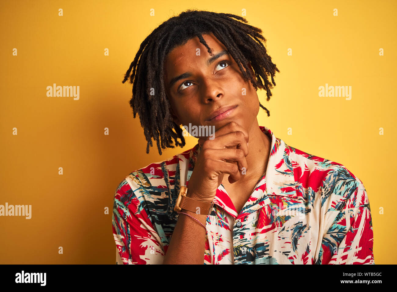 Afro man with dreadlocks on vacation wearing floral shirt over isolated yellow background ...