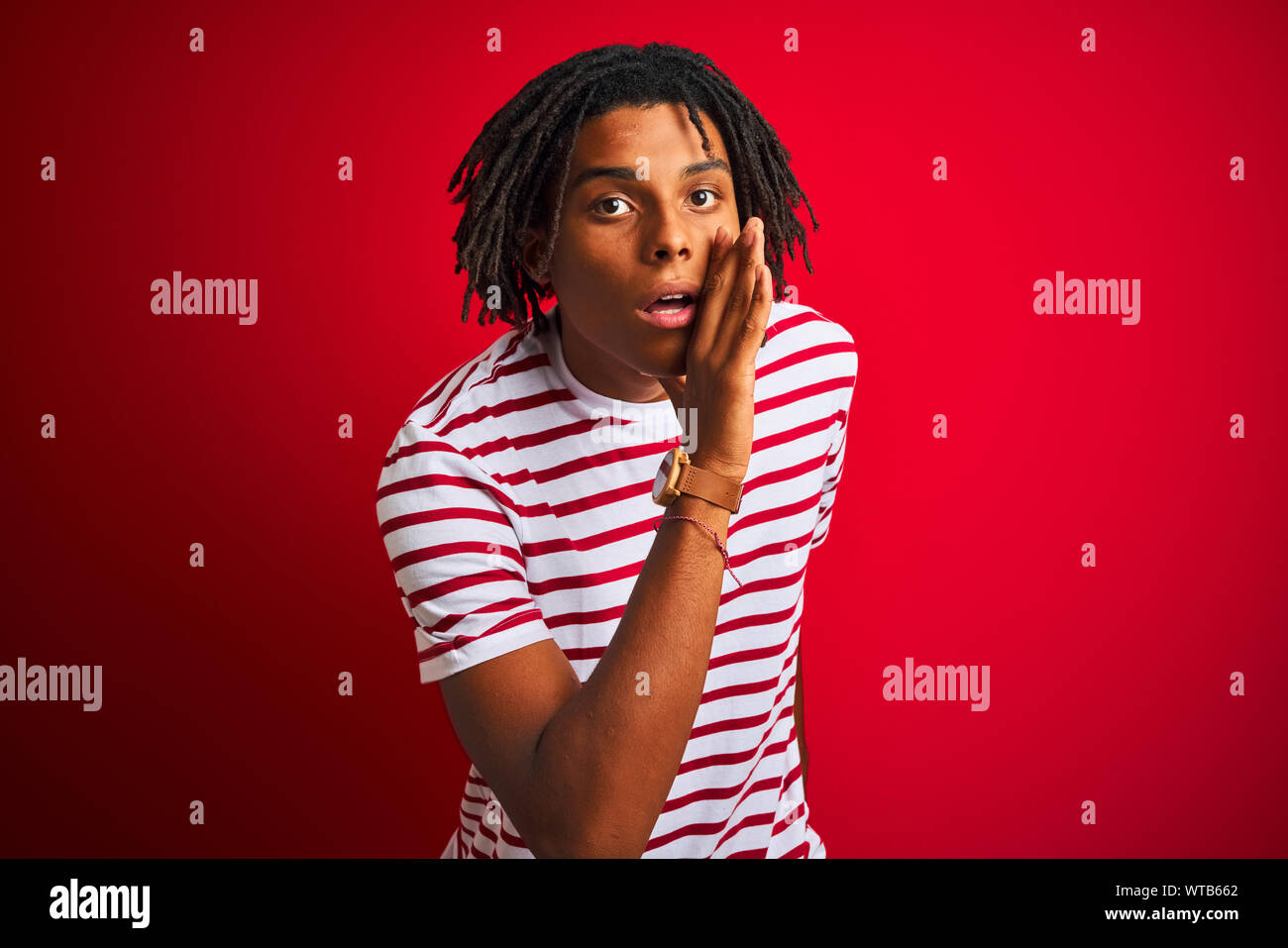 Young afro man with dreadlocks wearing striped t-shirt standing over ...