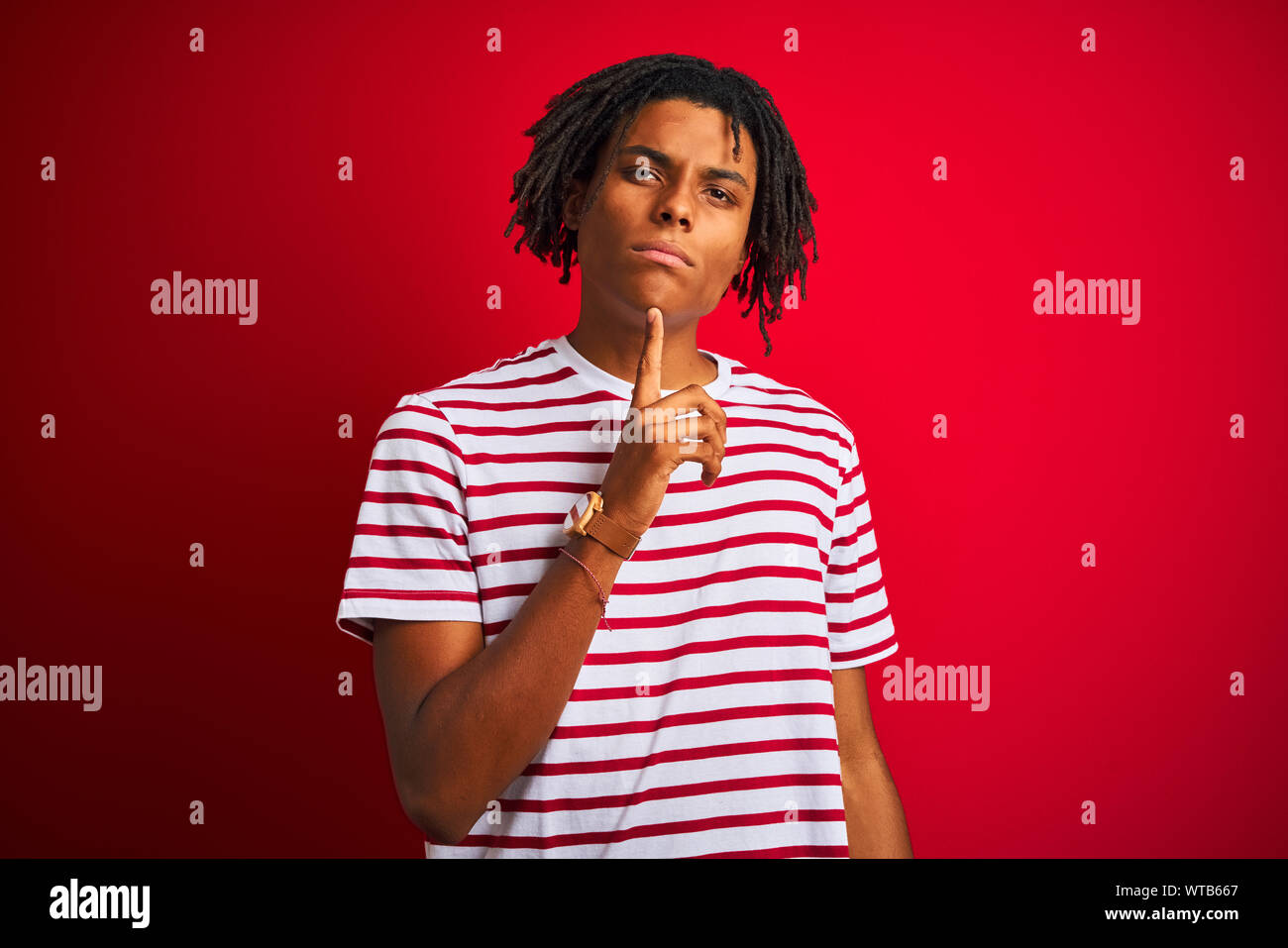 Young afro man with dreadlocks wearing striped t-shirt standing over ...