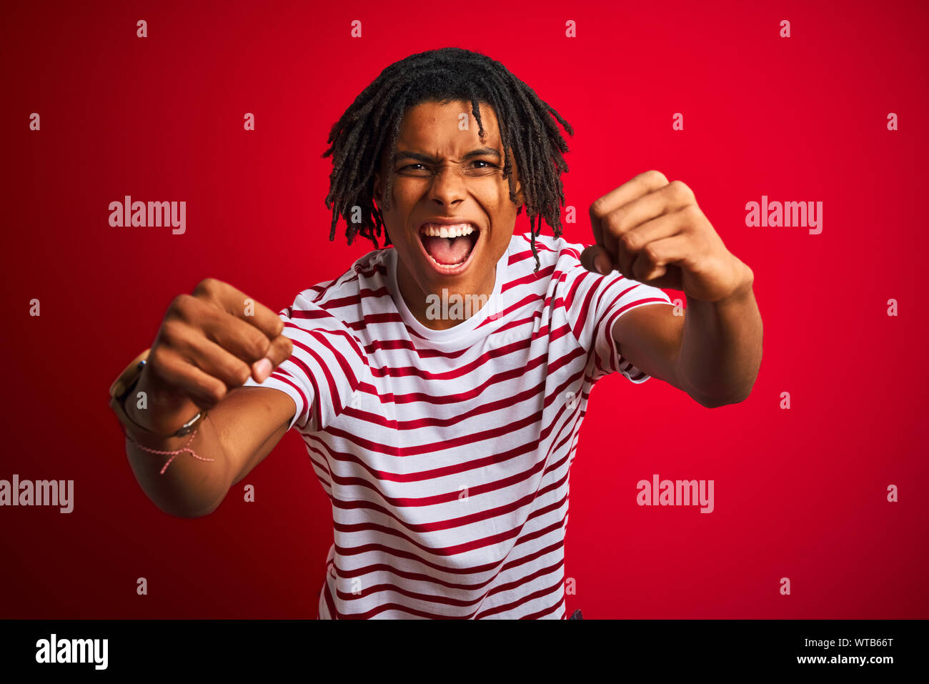 Young afro man with dreadlocks wearing striped t-shirt standing over ...