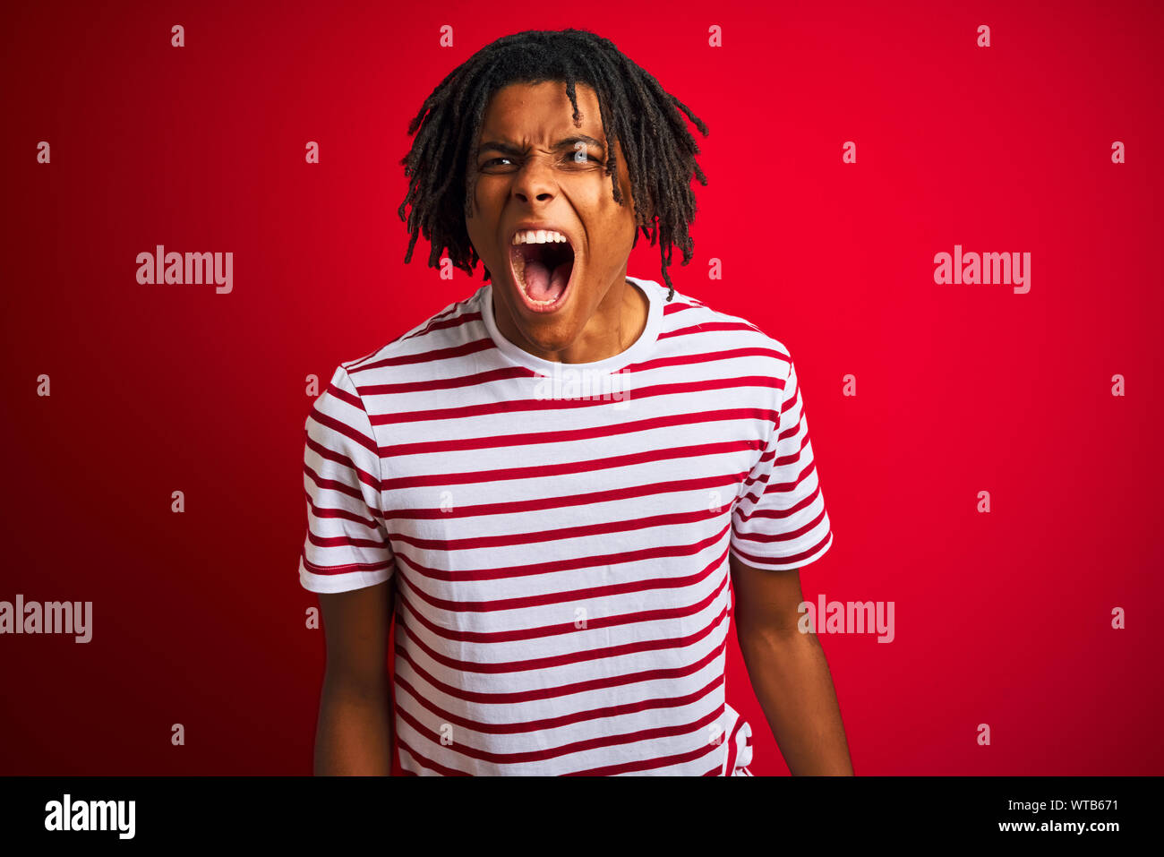 Young afro man with dreadlocks wearing striped t-shirt standing over ...