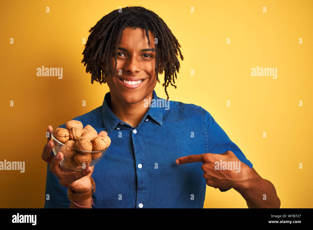 Afro american man with dreadlocks eating walnuts over isolated yellow ...