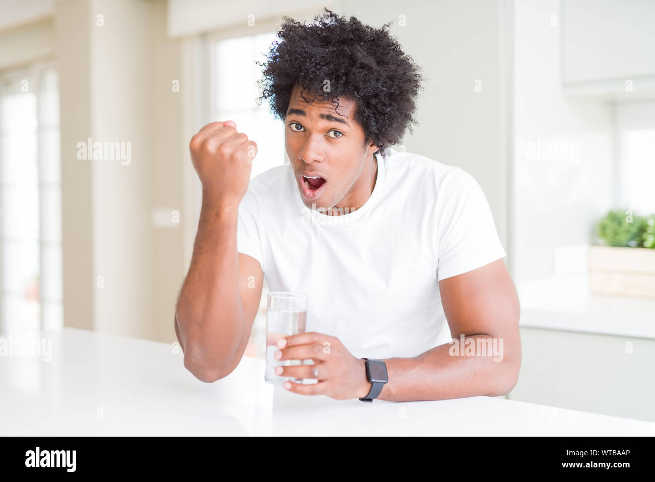African American man drinking a glass of water at home annoyed and ...