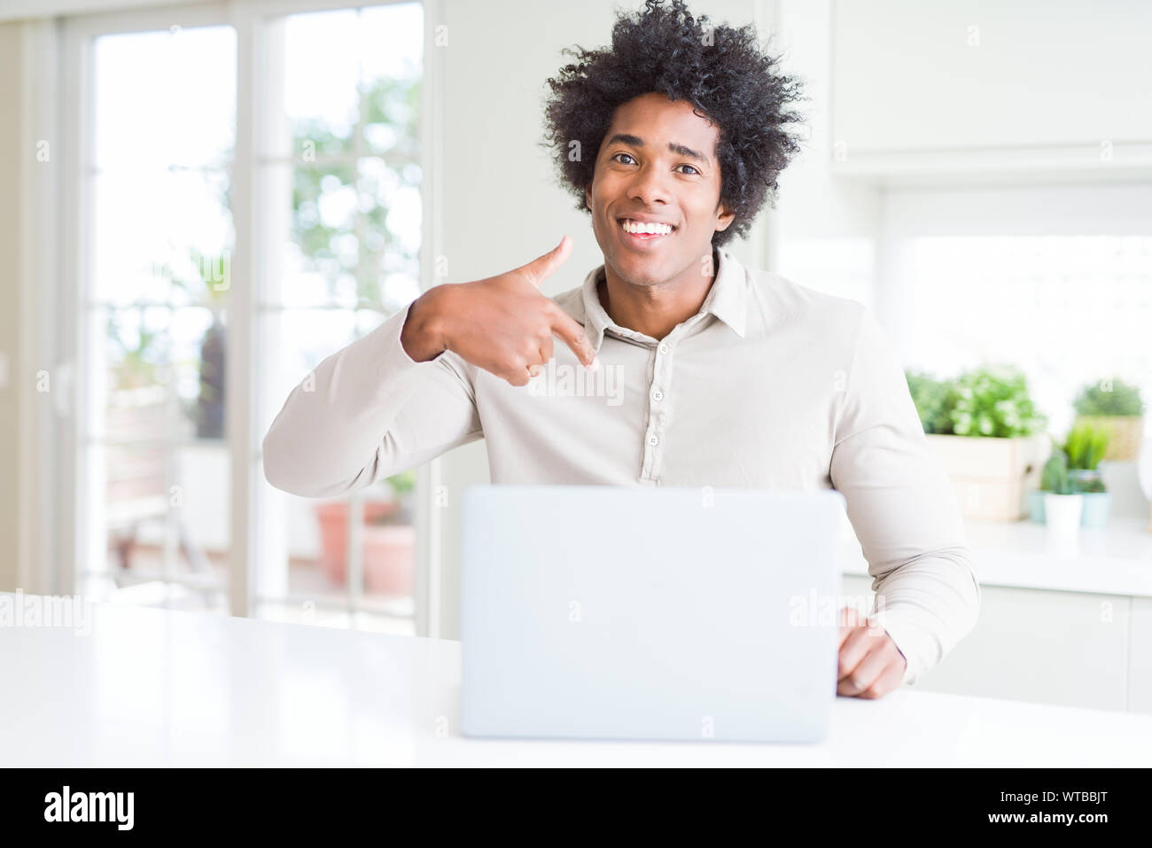 African American man working using laptop with surprise face pointing ...