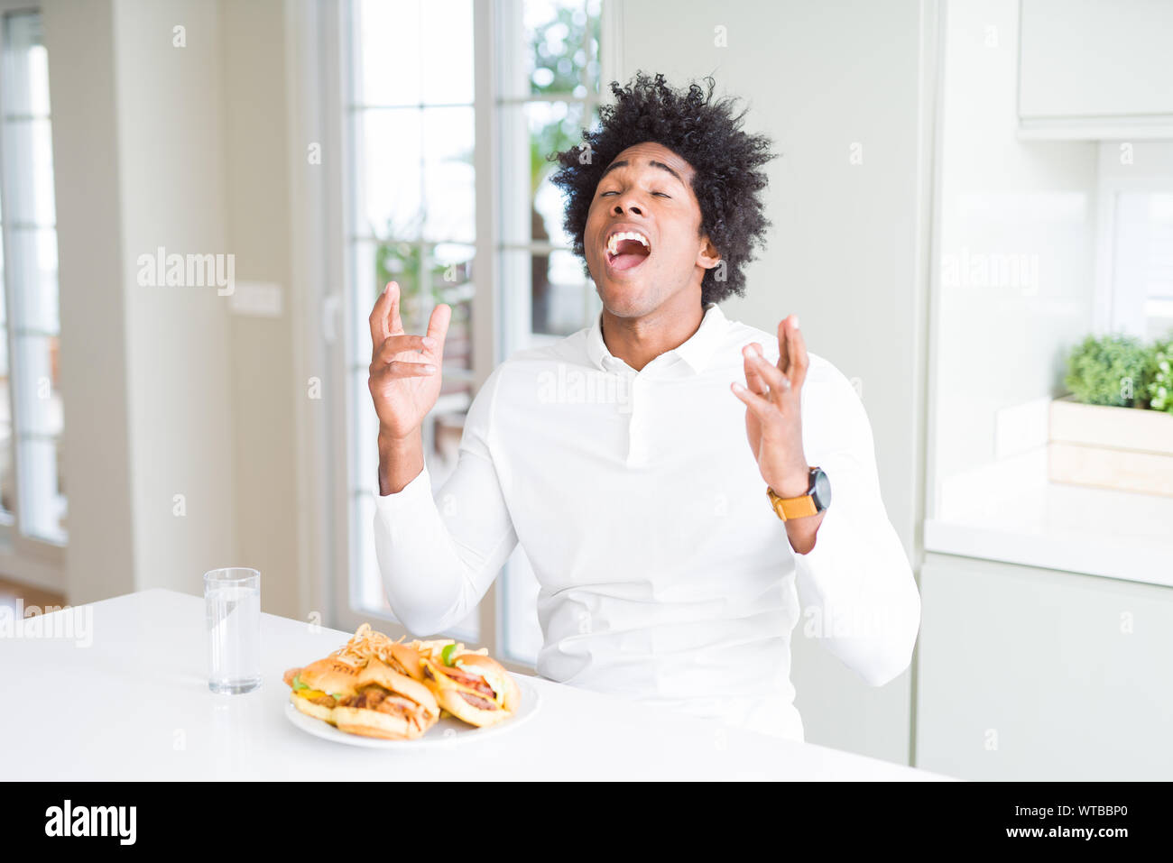 African American hungry man eating hamburger for lunch celebrating mad ...