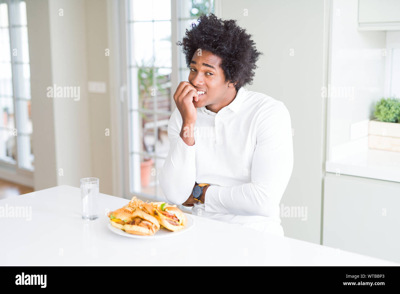 African American hungry man eating hamburger for lunch looking stressed ...