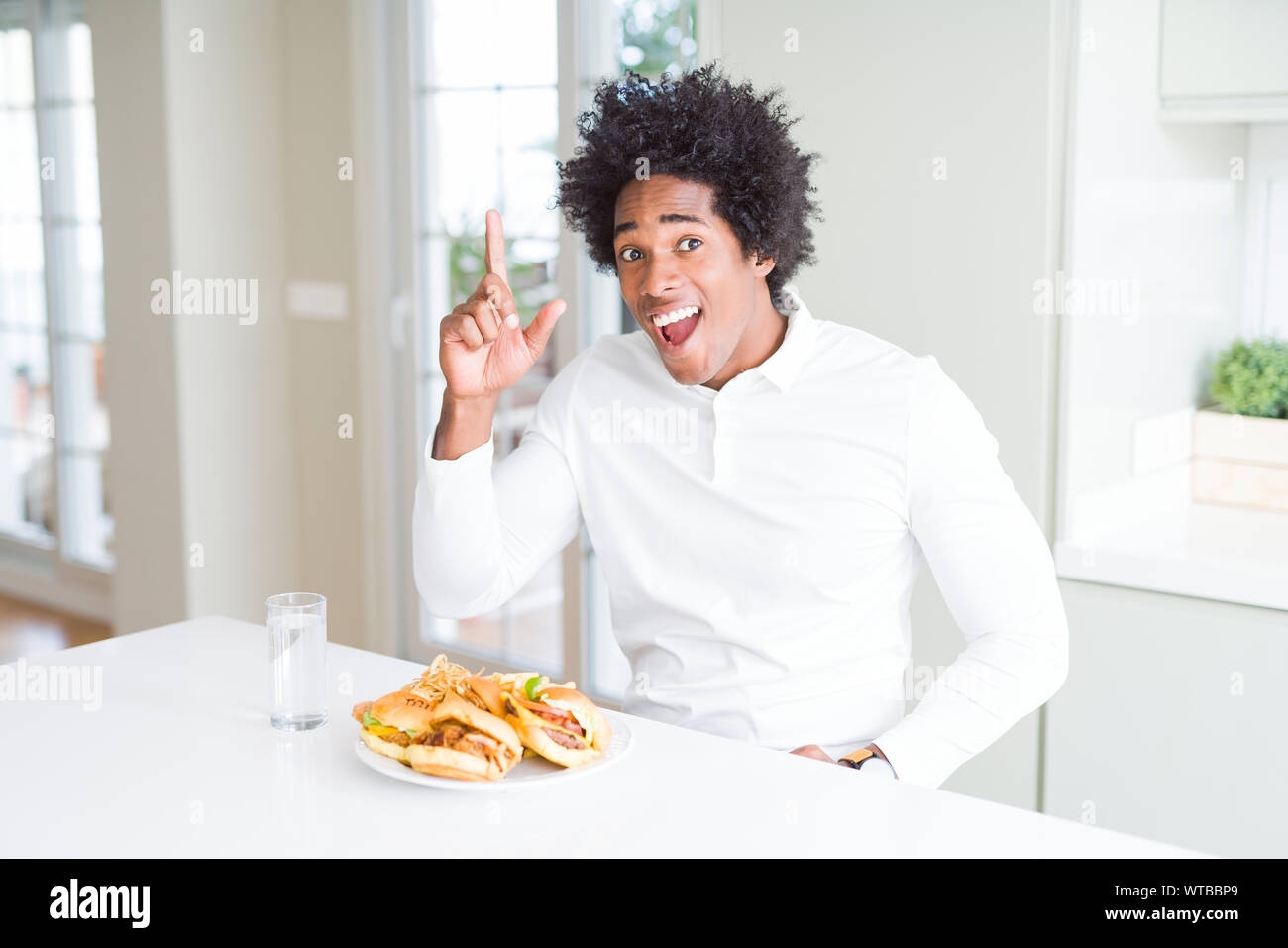 African American hungry man eating hamburger for lunch pointing finger ...