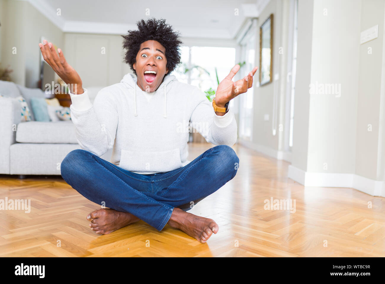 African American man sitting on the floor at home celebrating crazy and ...