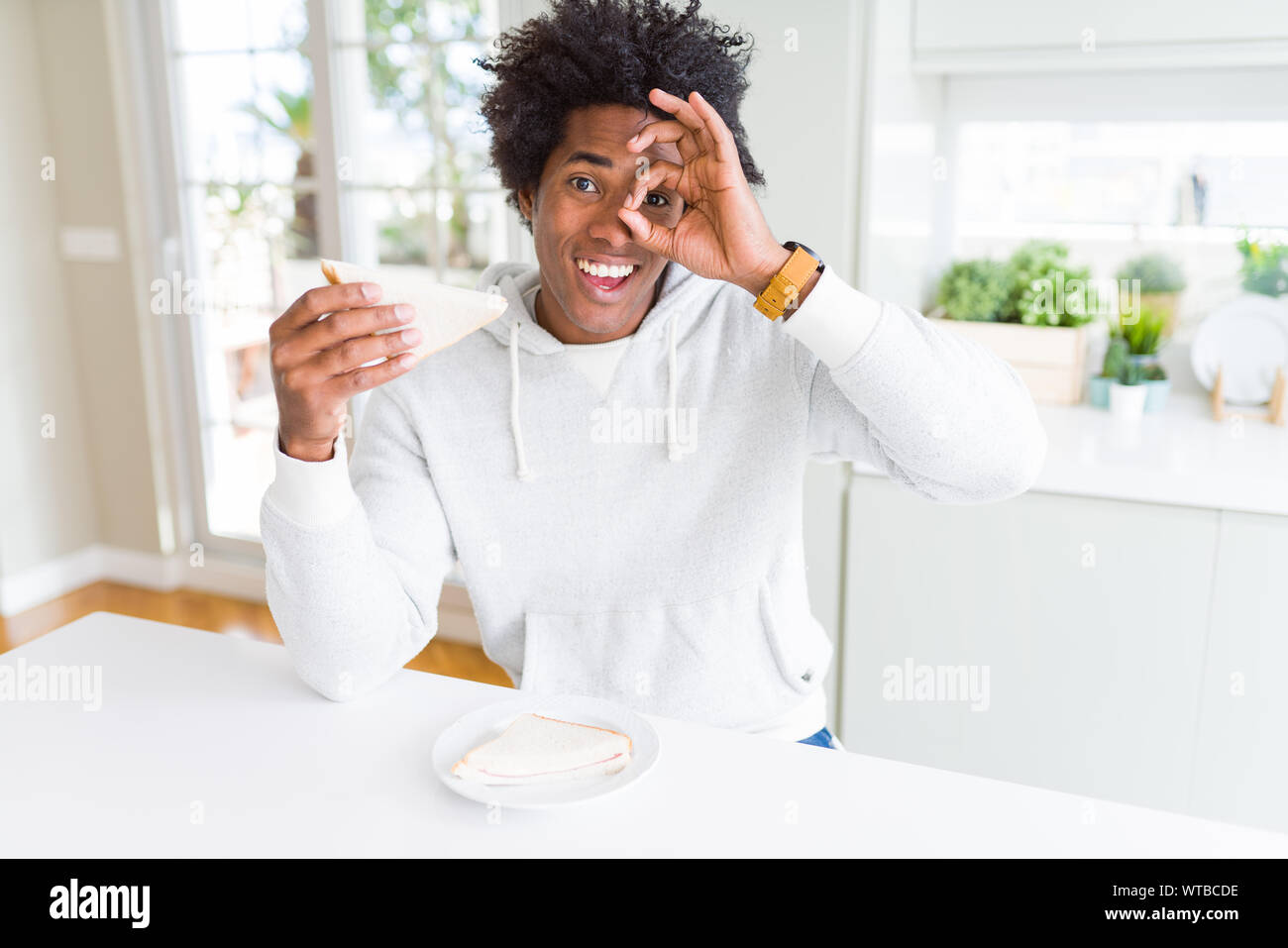 African American man eating handmade sandwich at home with happy face ...