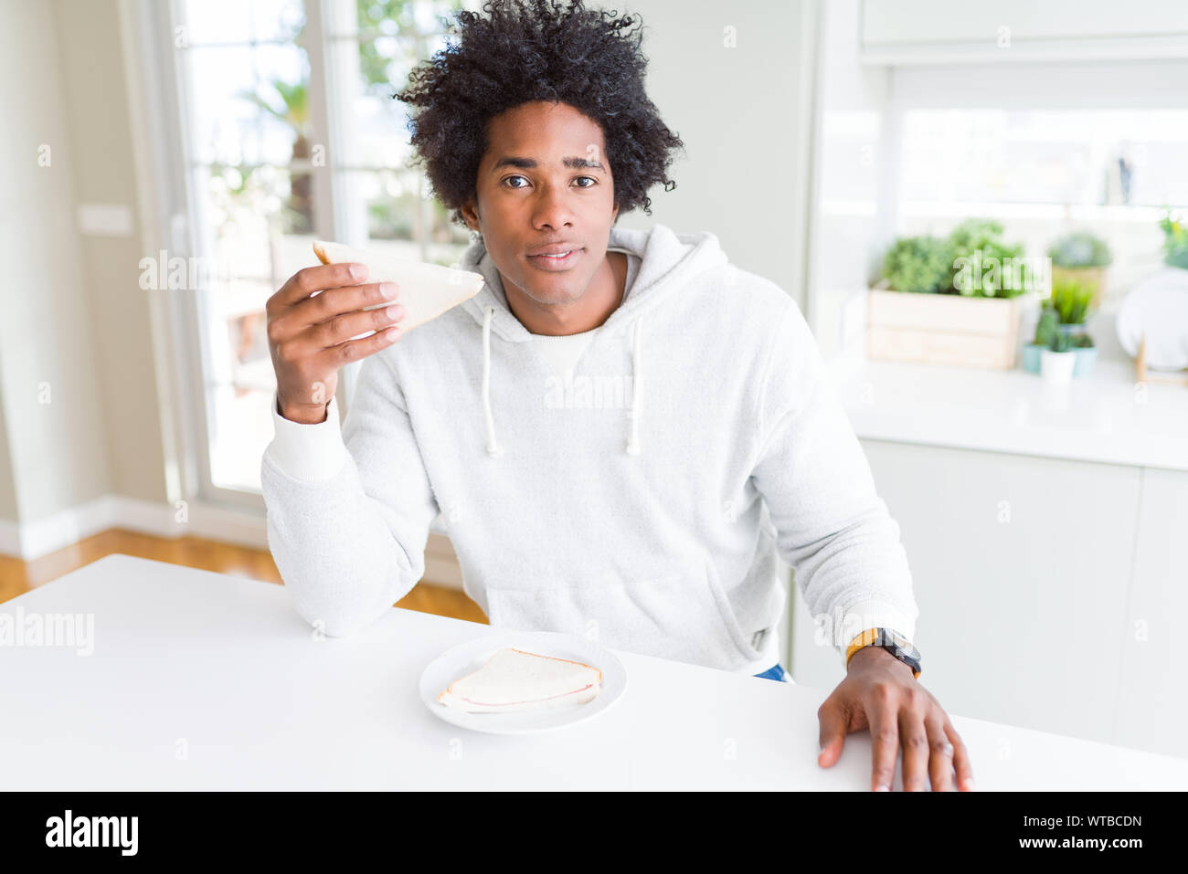 African American man eating handmade sandwich at home with a confident ...