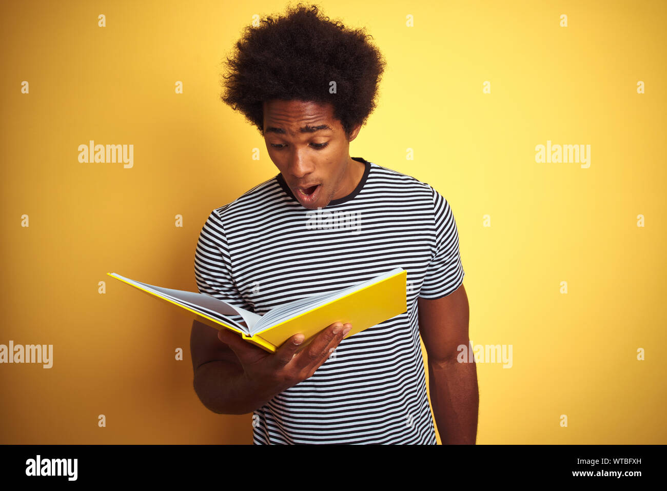 Afro american student man reading book standing over isolated yellow ...