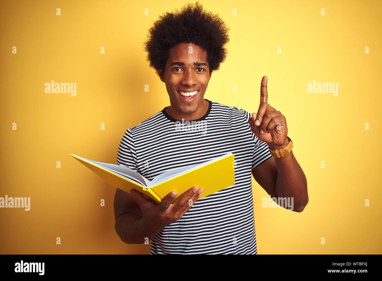 Afro american student man reading book standing over isolated yellow ...