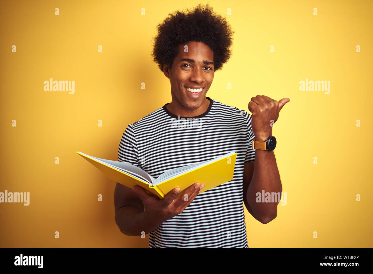 Afro american student man reading book standing over isolated yellow ...