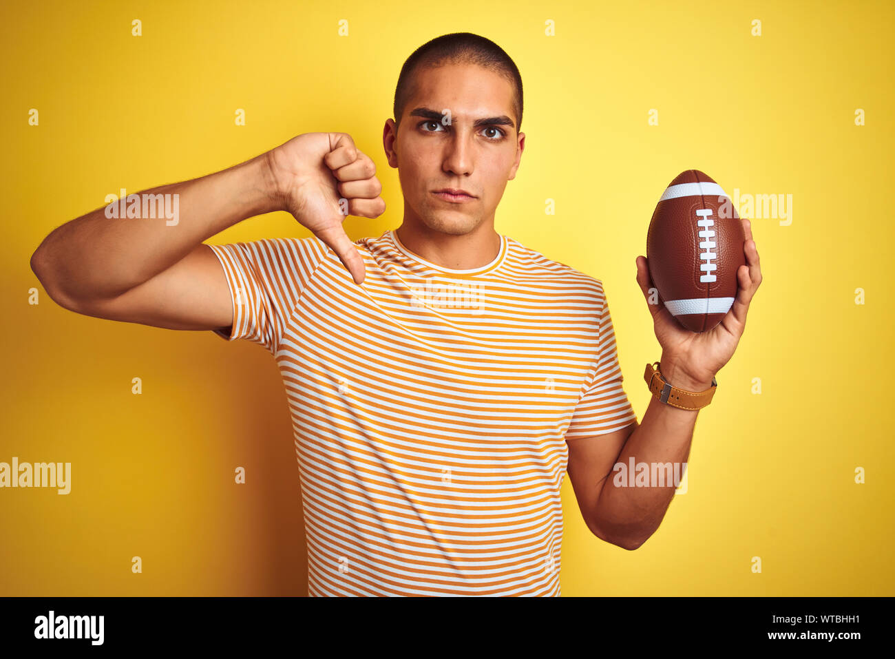 Young rugby player man holding a football ball over yellow isolated ...