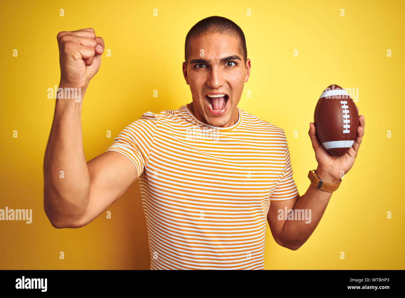 Young rugby player man holding a football ball over yellow isolated ...