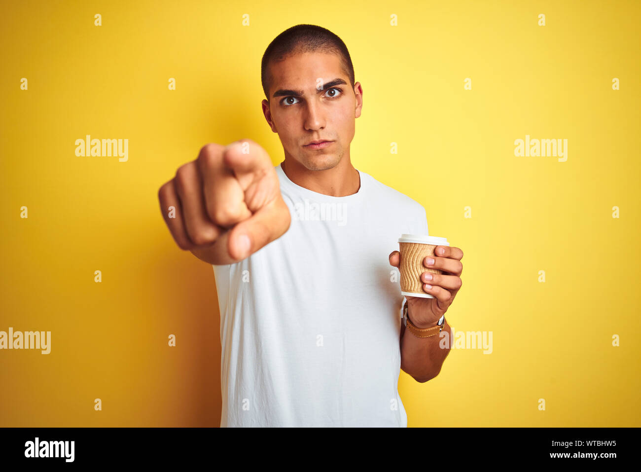 Young handsome man drinking a take away glass of coffee over yellow ...