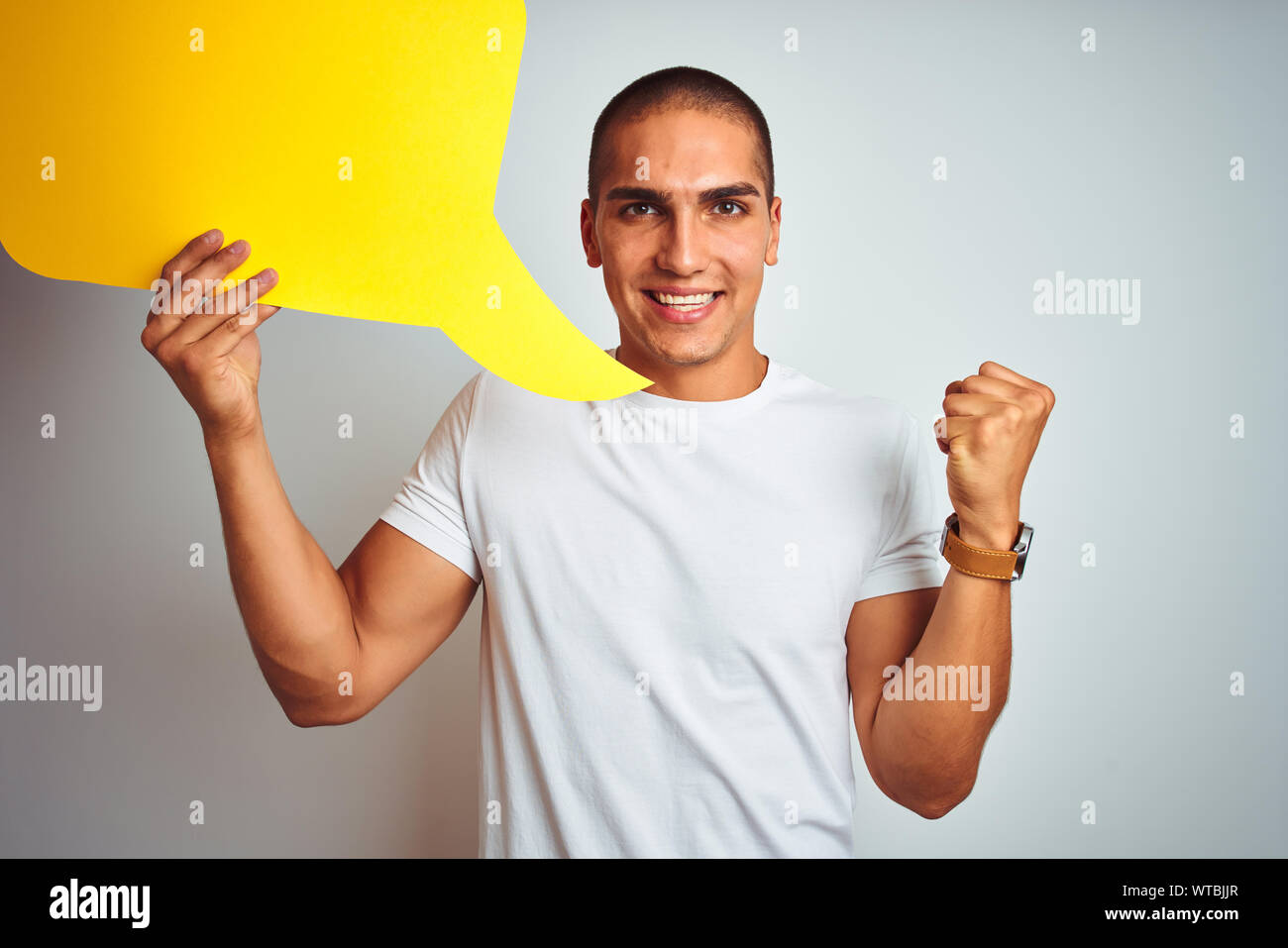 Young man holding yellow speech bubble over white isolated background ...