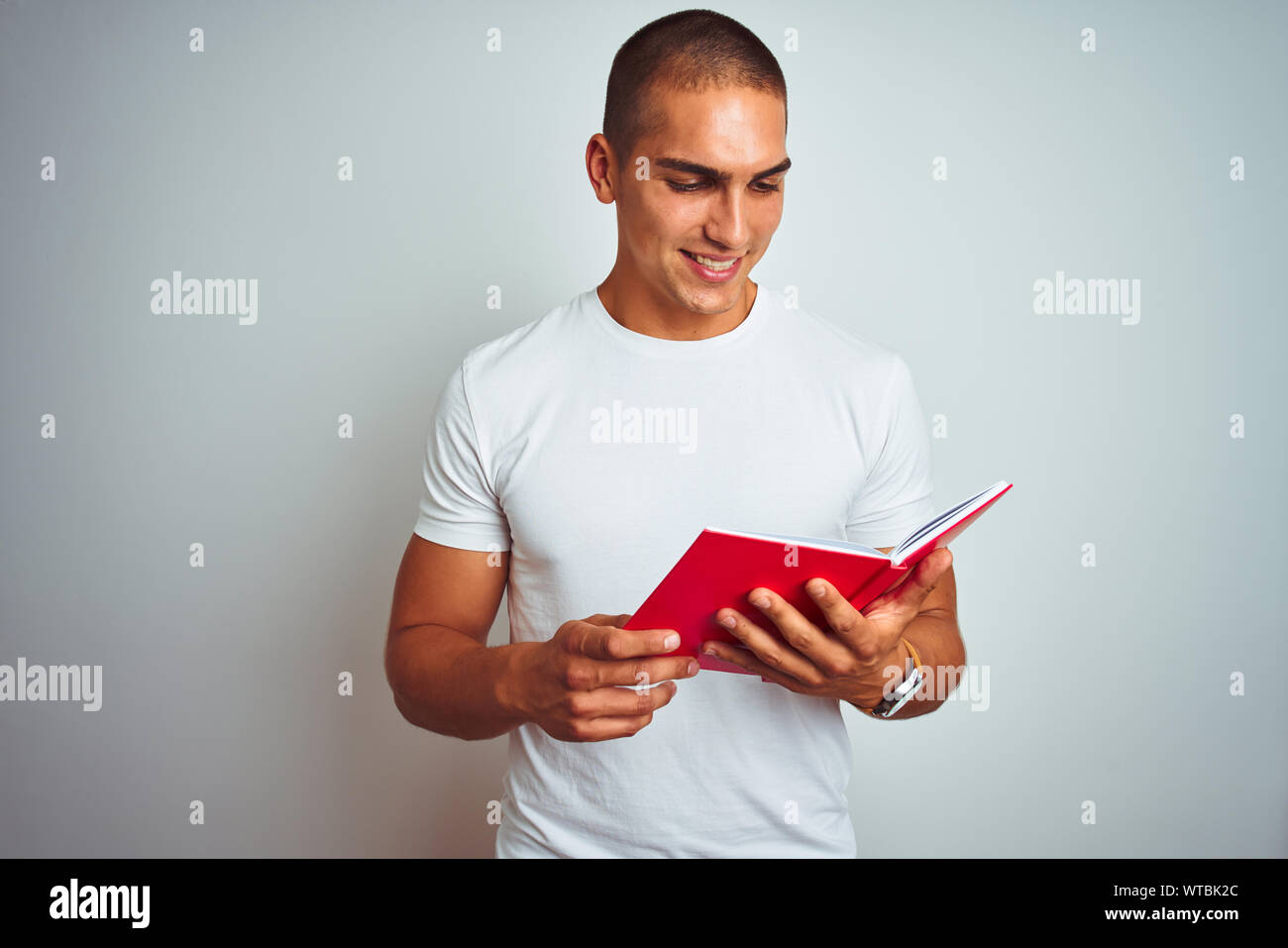 Young handsome man reading red book over white isolated background with ...