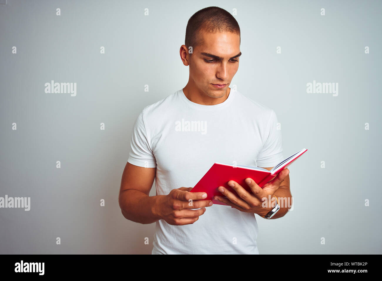 Young handsome man reading red book over white isolated background with ...