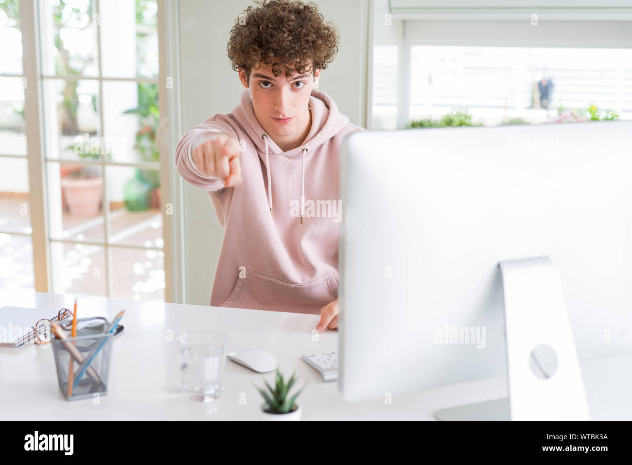 Young student man using computer pointing with finger to the camera and ...