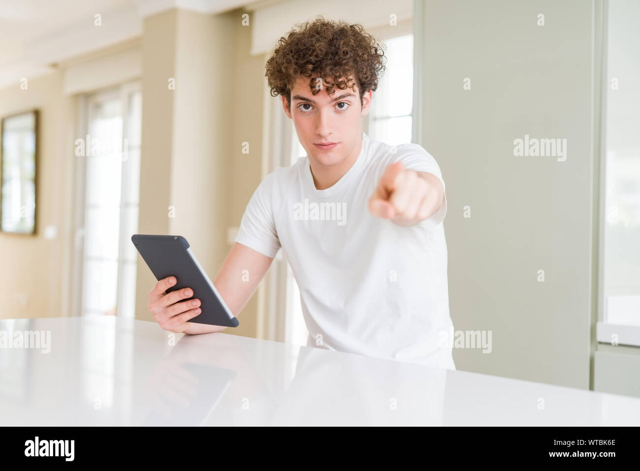 Young man using touchpad tablet pointing with finger to the camera and ...