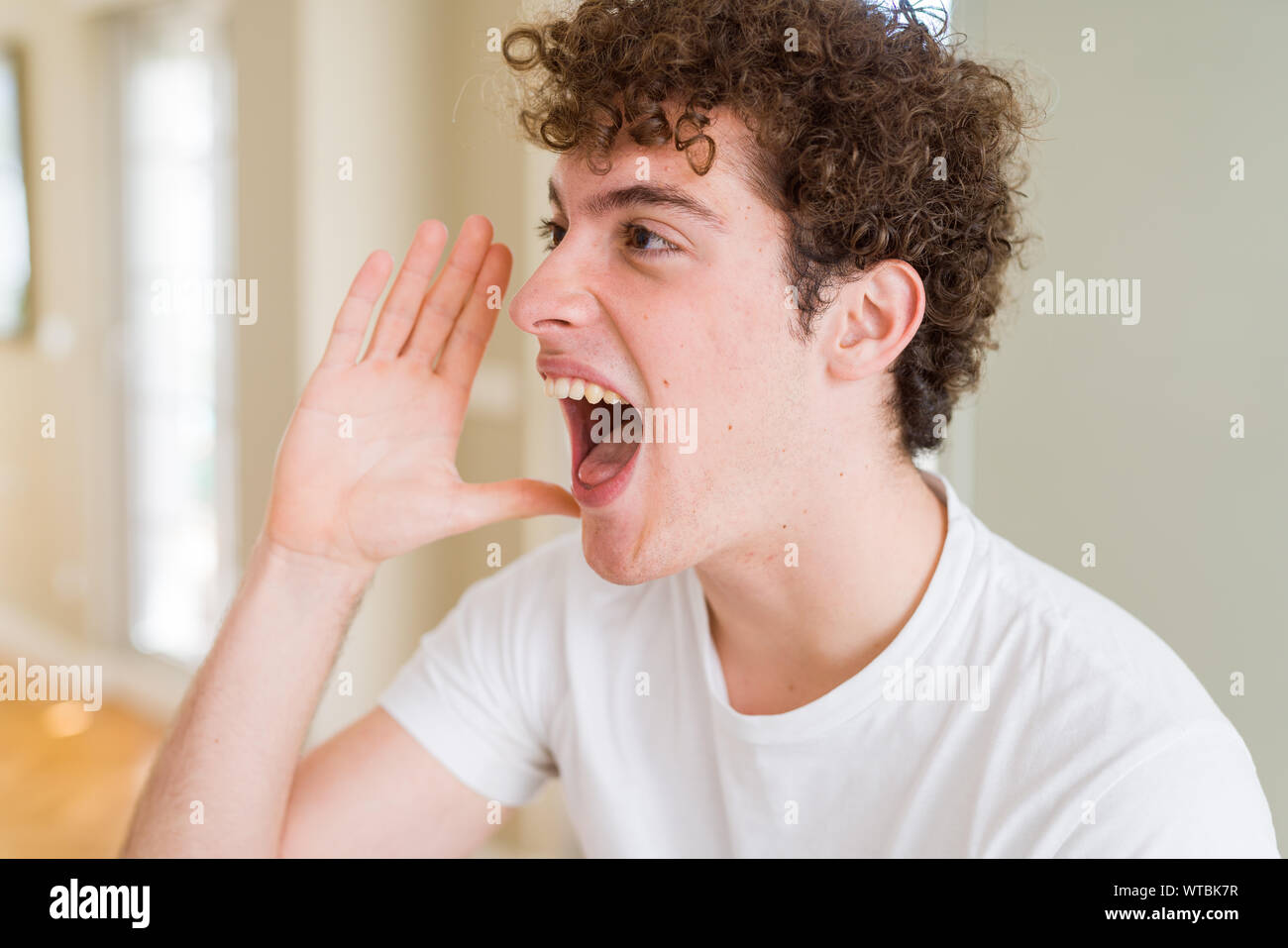 Young handsome man wearing white t-shirt shouting and screaming loud to ...