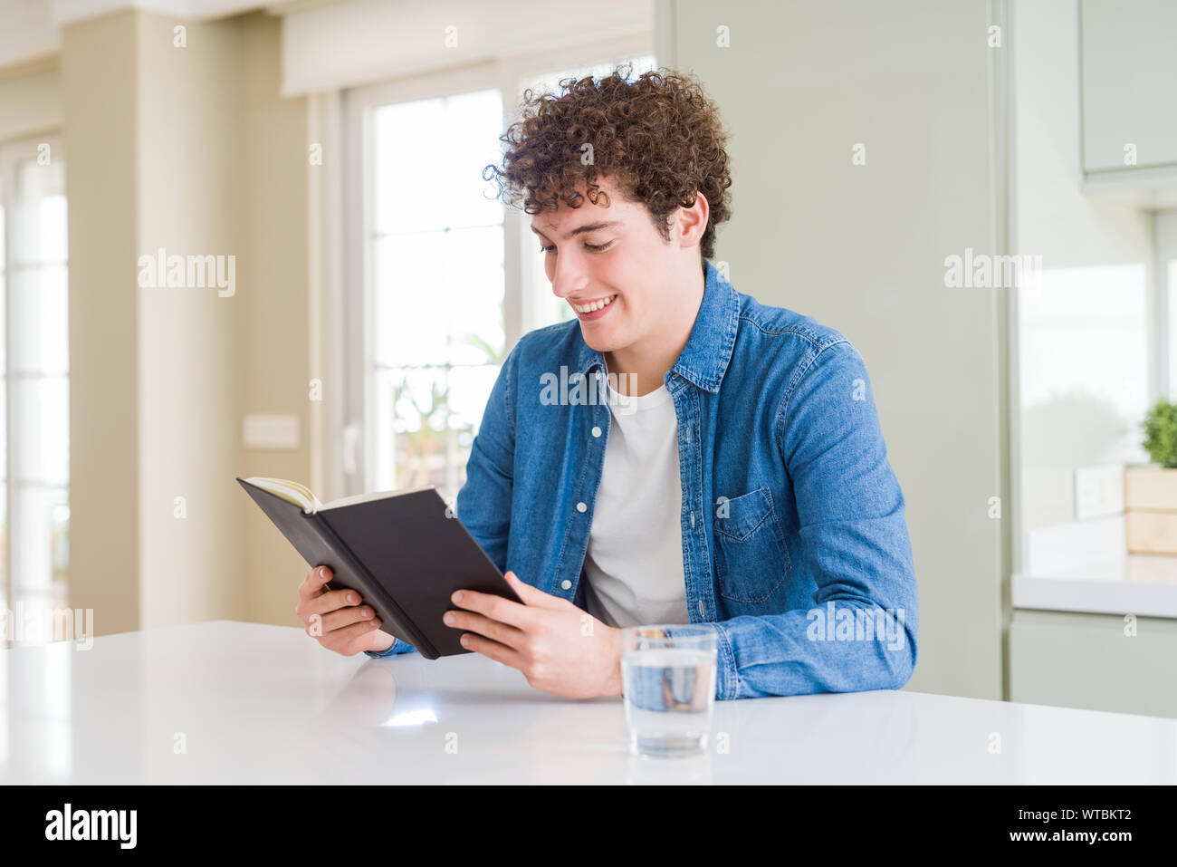 Young man reading a book at home with a happy face standing and smiling ...