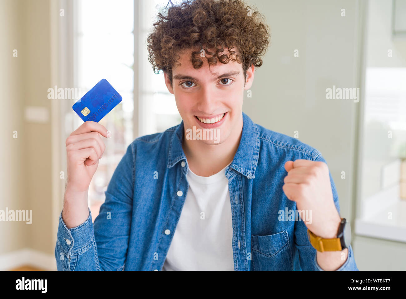Young man holding credit card screaming proud and celebrating victory ...