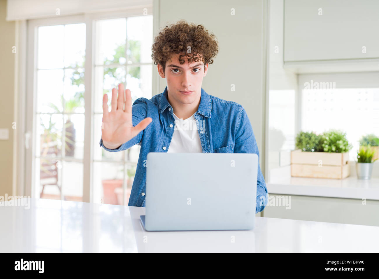 Young man using computer laptop with open hand doing stop sign with ...