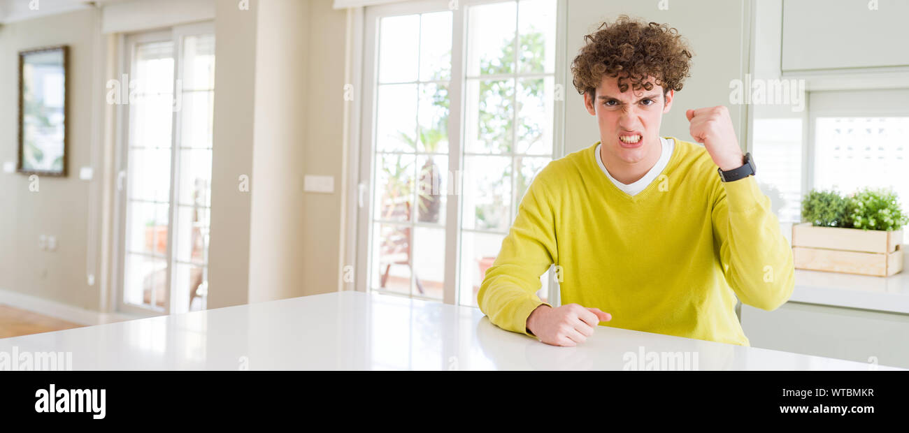Wide angle shot of young handsome man at home angry and mad raising ...