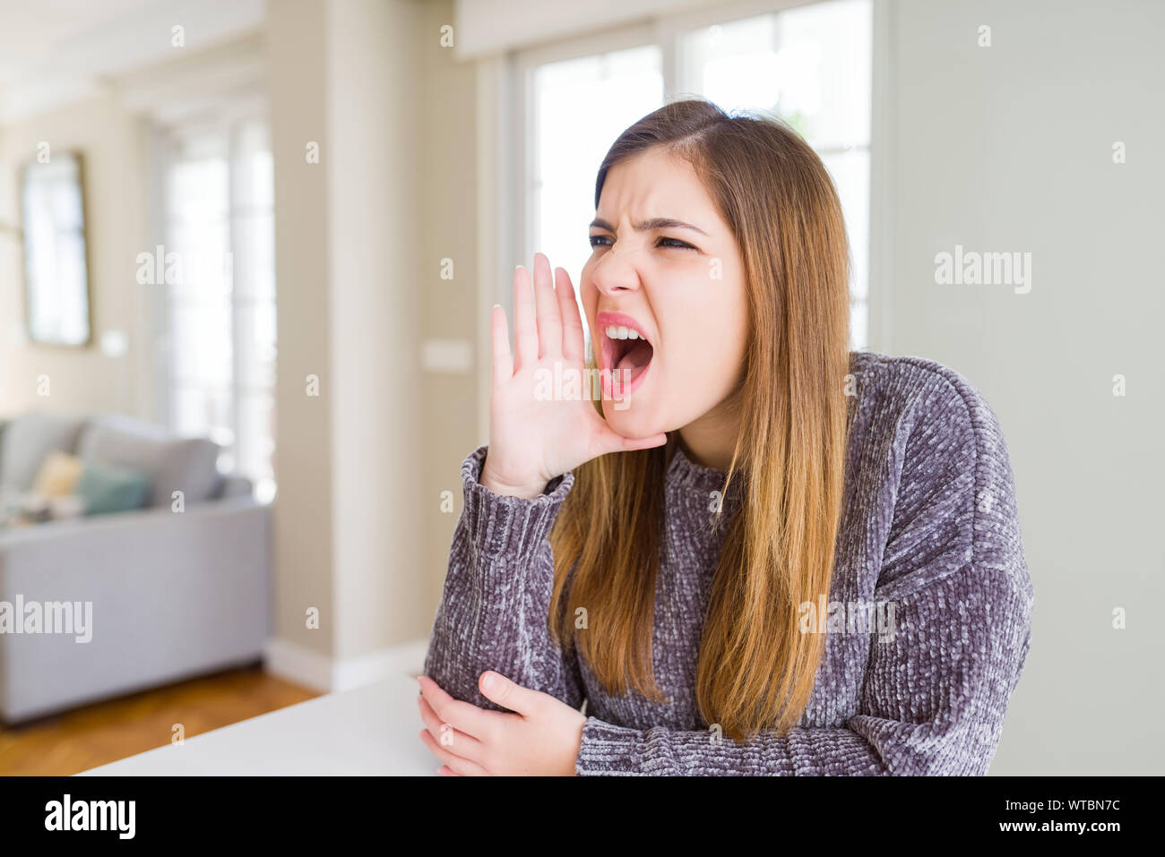 Beautiful young woman at home shouting and screaming loud to side with ...