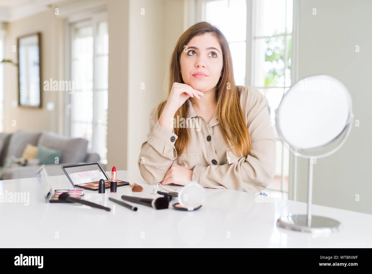 Beautiful young woman using make up cosmetics with hand on chin ...