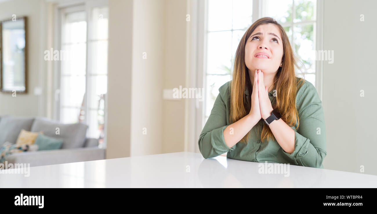 Beautiful young woman at home begging and praying with hands together ...