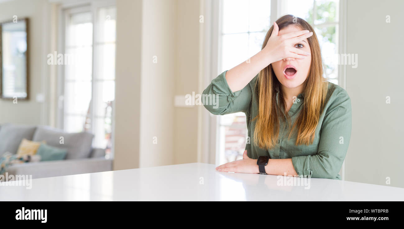Beautiful young woman at home peeking in shock covering face and eyes ...