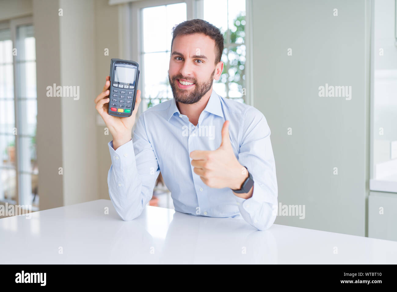 Handsome young man holding point of sale terminal happy with big smile ...