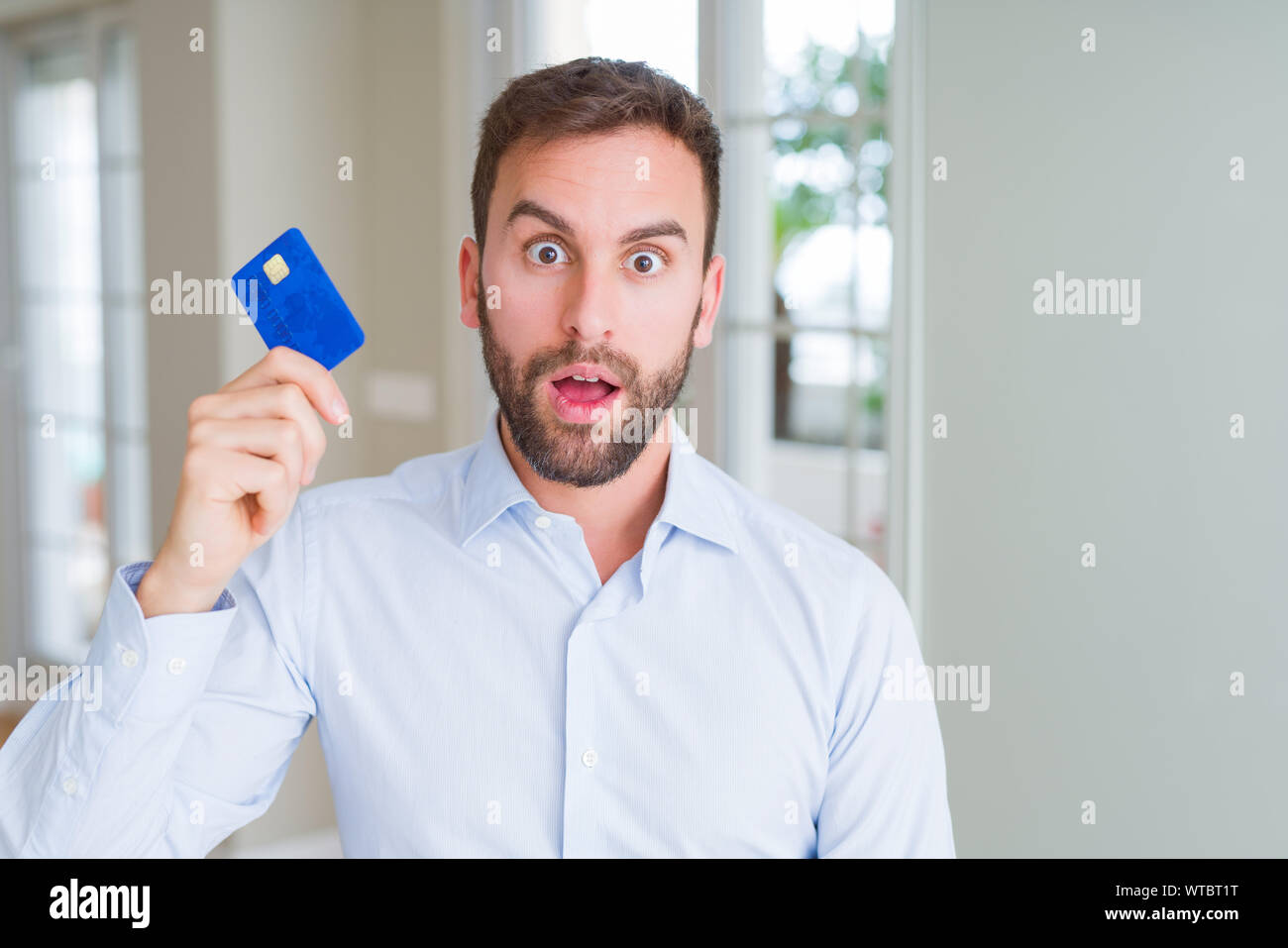 Handsome business man holding credit card scared in shock with a ...