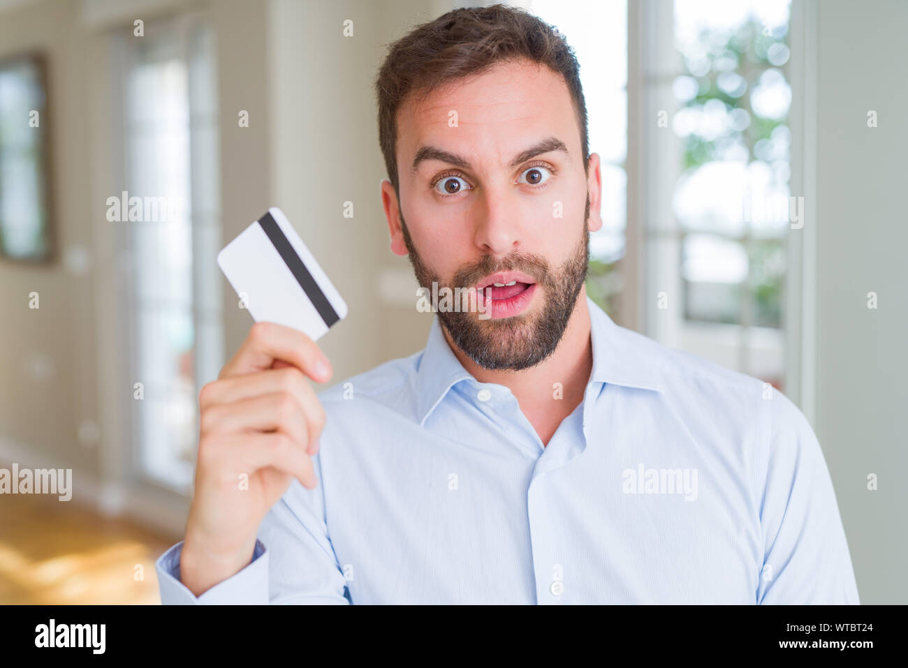 Handsome business man holding credit card scared in shock with a ...