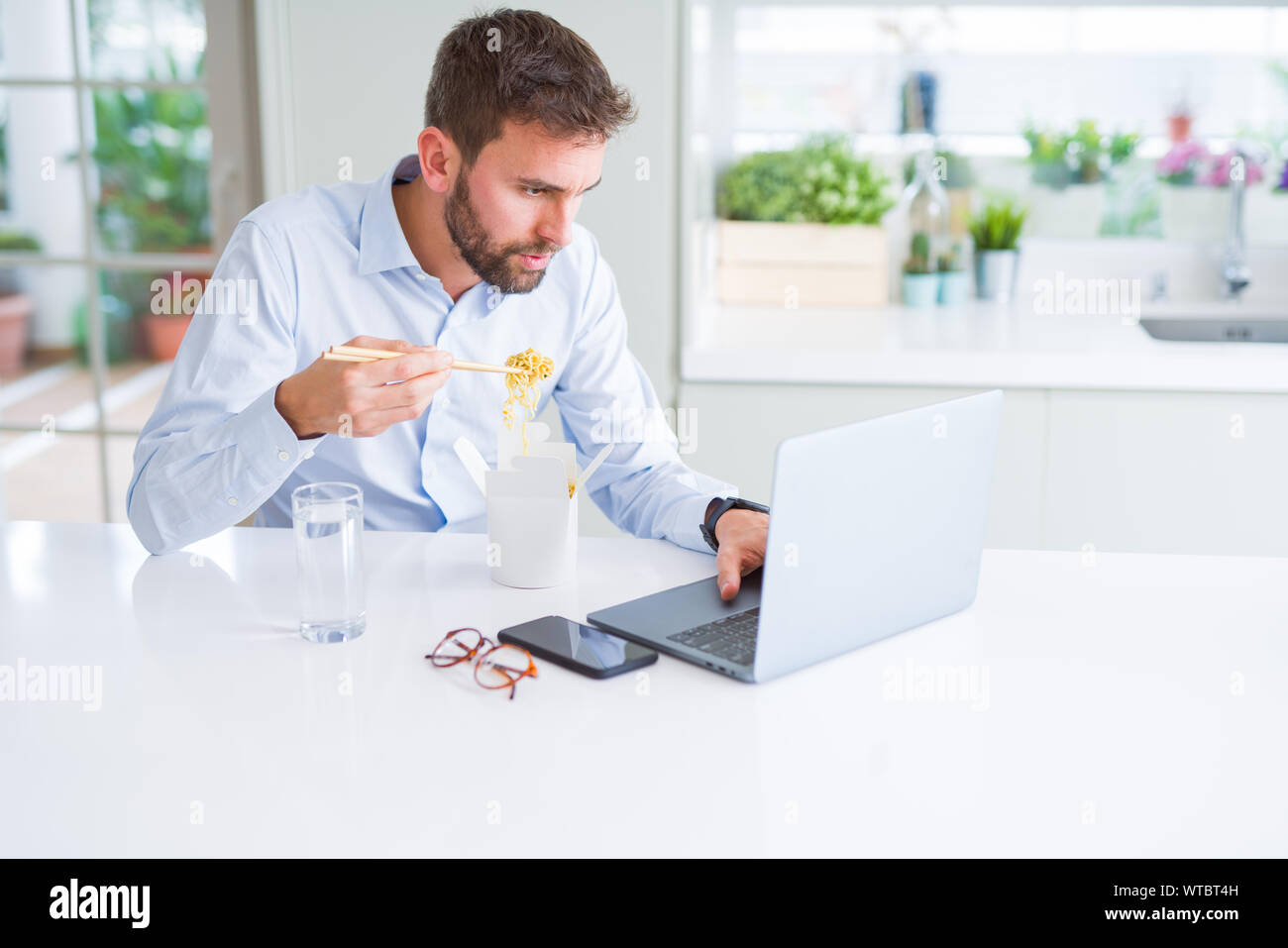 Business man eating take away asian noodles food while working using ...