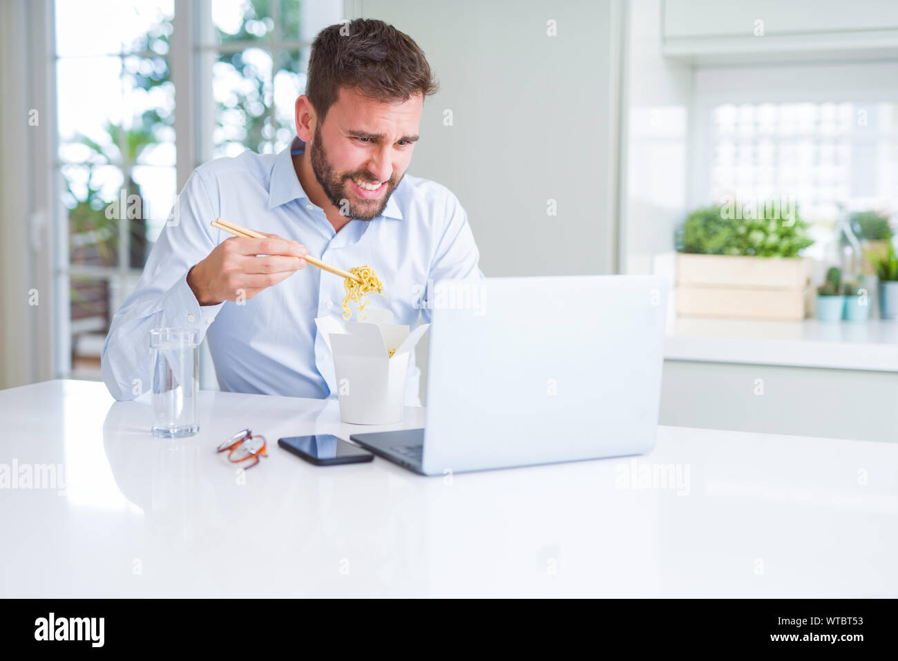 Business man eating take away asian noodles food while working using ...